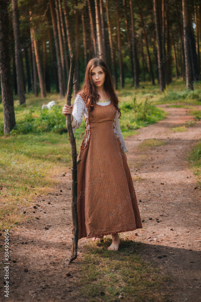 Young beautiful girl in medieval cowboy clothes, with a stick in hand ...