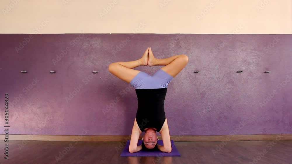 Yoga practitioner doing baddha konasana in sirsasana on purple mat at ...