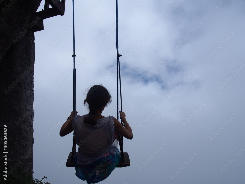 A young woman sitting on a large wooden swing at the treehouse under a ...