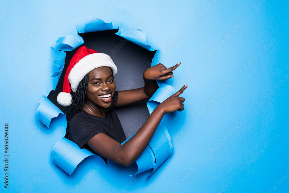 Young african woman wear in santa hat pointed with hand on copy space ...