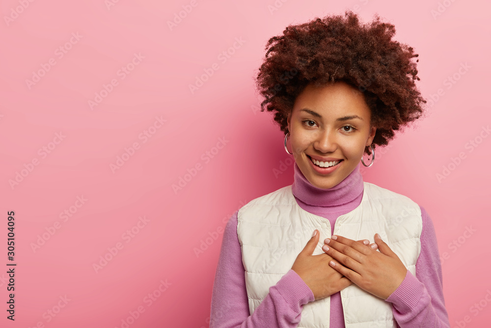 Positive Afro woman presses hands on chest, appreciates heartwarming ...