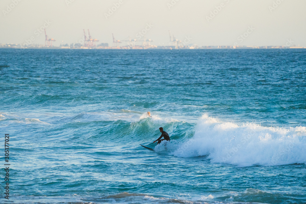 Surfers out in the evening, catching a surf on the waves with the sun ...