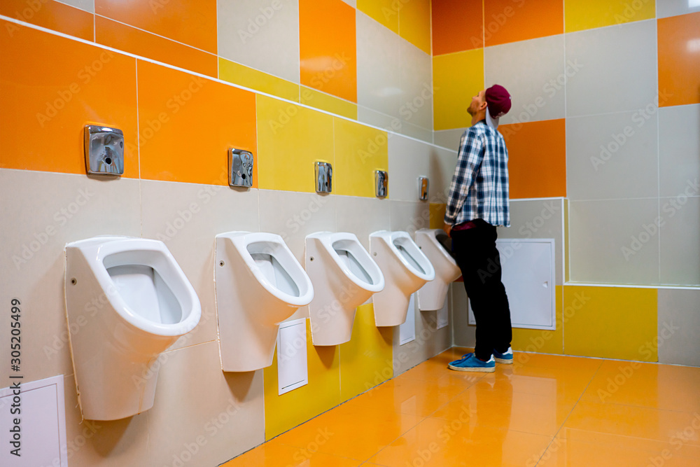 young man in the public toilet, standing next to the urinal in the ...