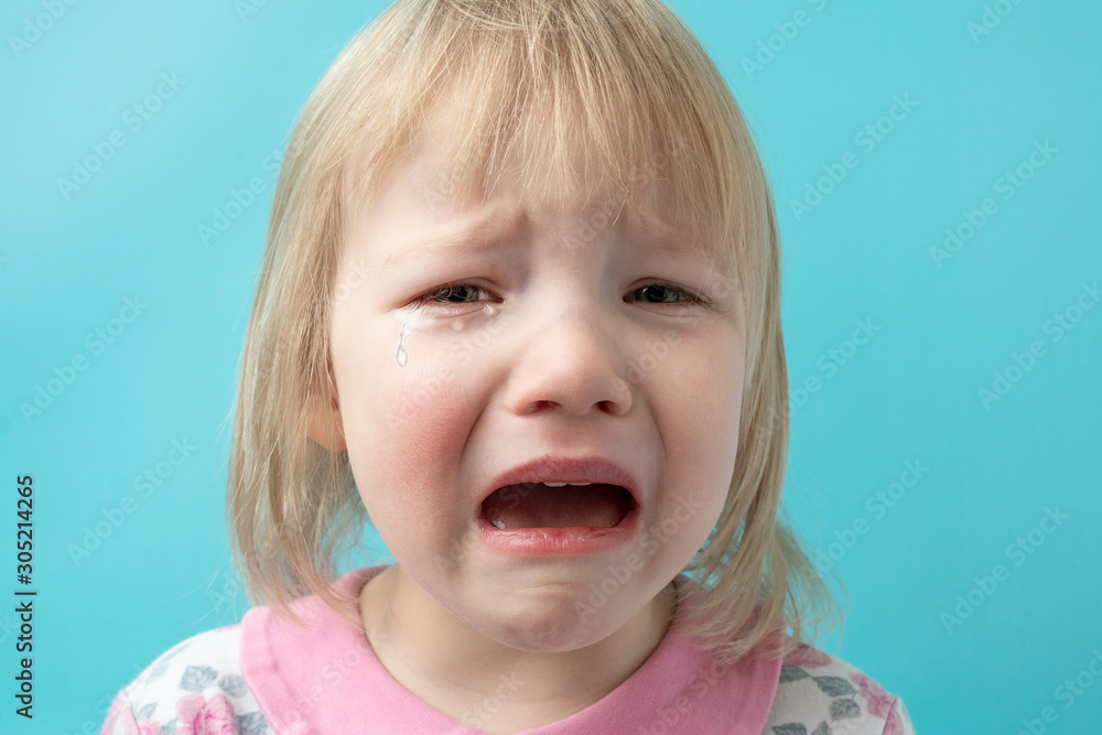 little girl in a pink dress on a blue background. the child cries with ...