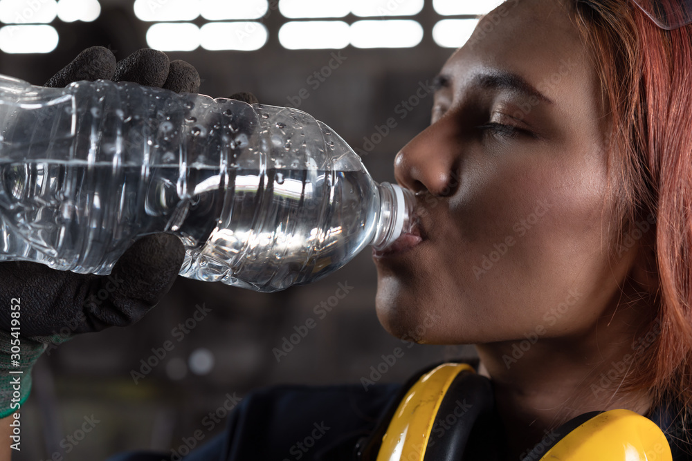 Female industrial engineer drinking water from bottle during work break ...