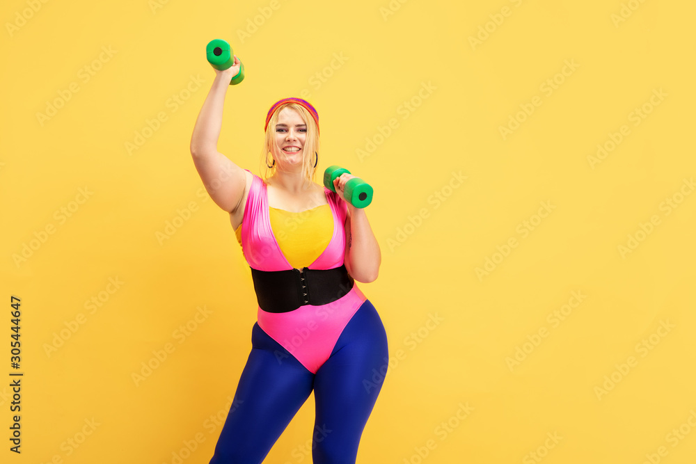 Young caucasian plus size female model's training on yellow background ...