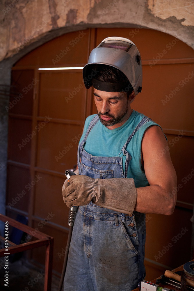 Professional man with welding mask on head wearing jeans overalls and ...