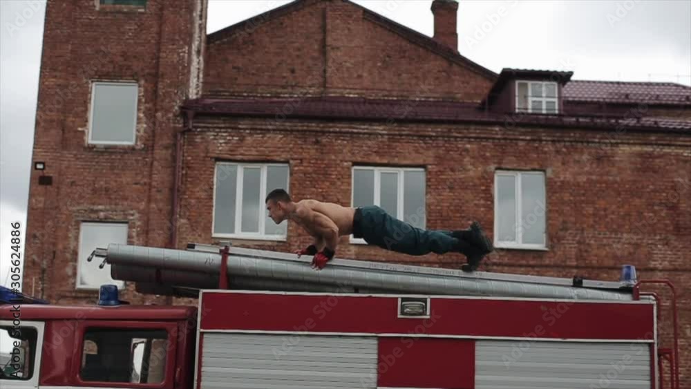 Strong shirtless firefighter doing push-ups with crossed legs on top of ...