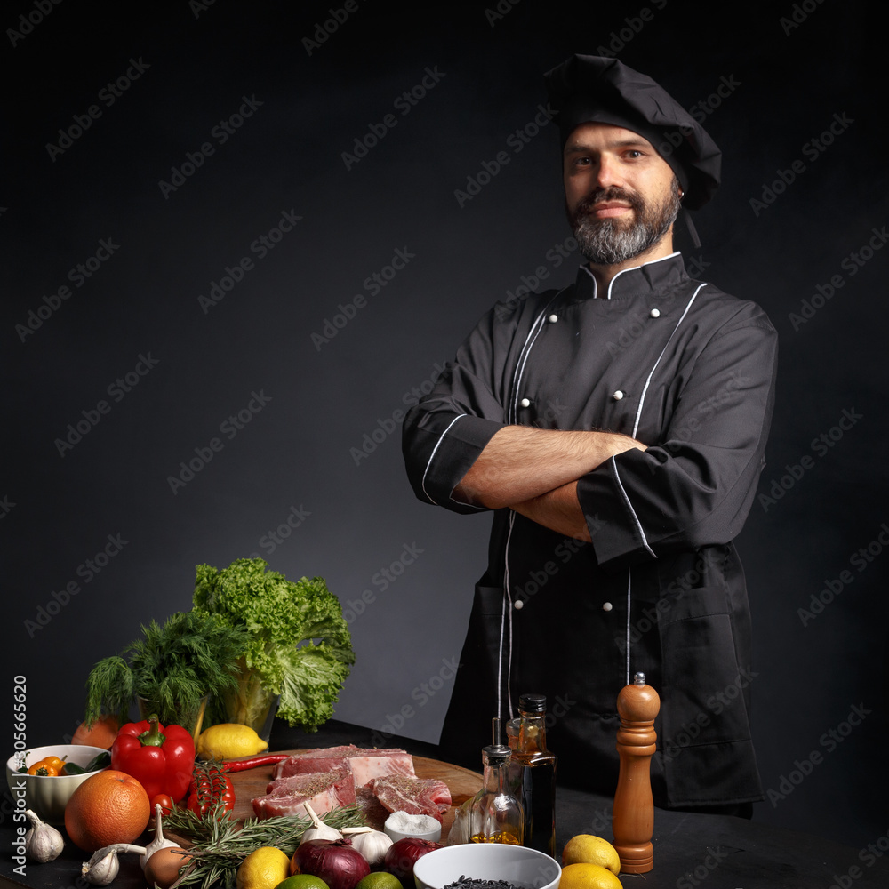 Foto de Male chef in black uniform posing near a table with groceries ...