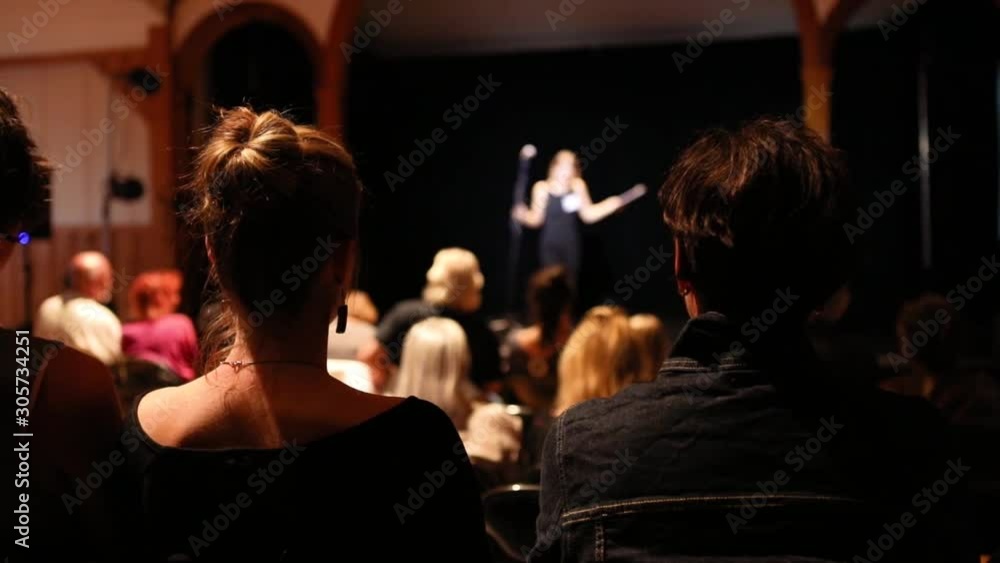 View from the back of audience applauding female speaker in a theater ...