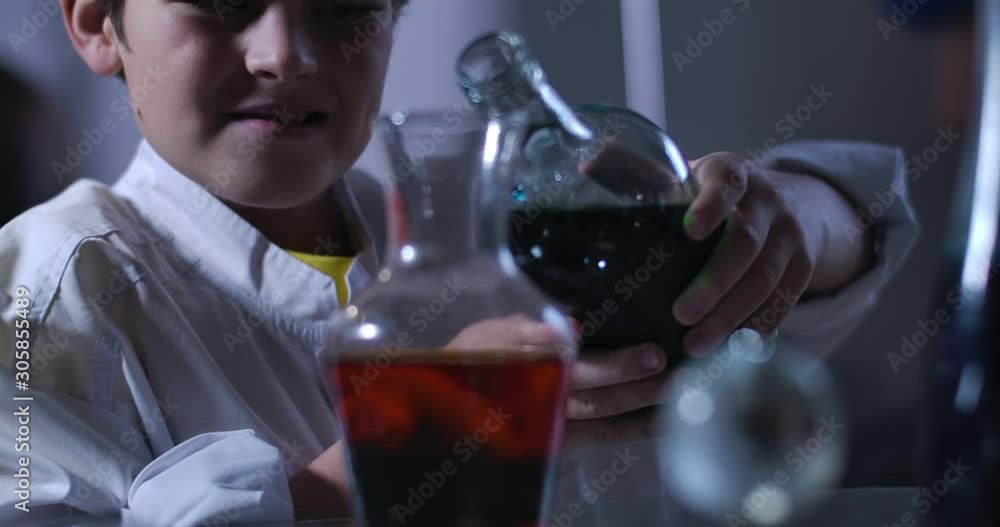 Close-up face of Caucasian boy mixing black and red chemical reagents ...