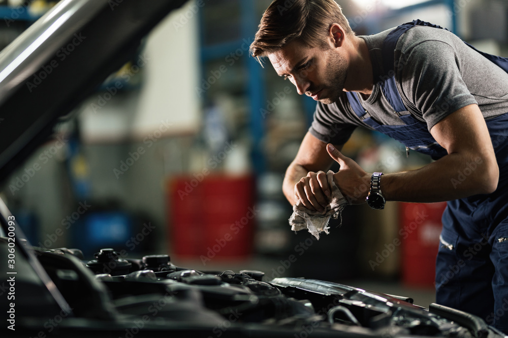 Young auto mechanic cleaning hands after working on car engine in a ...