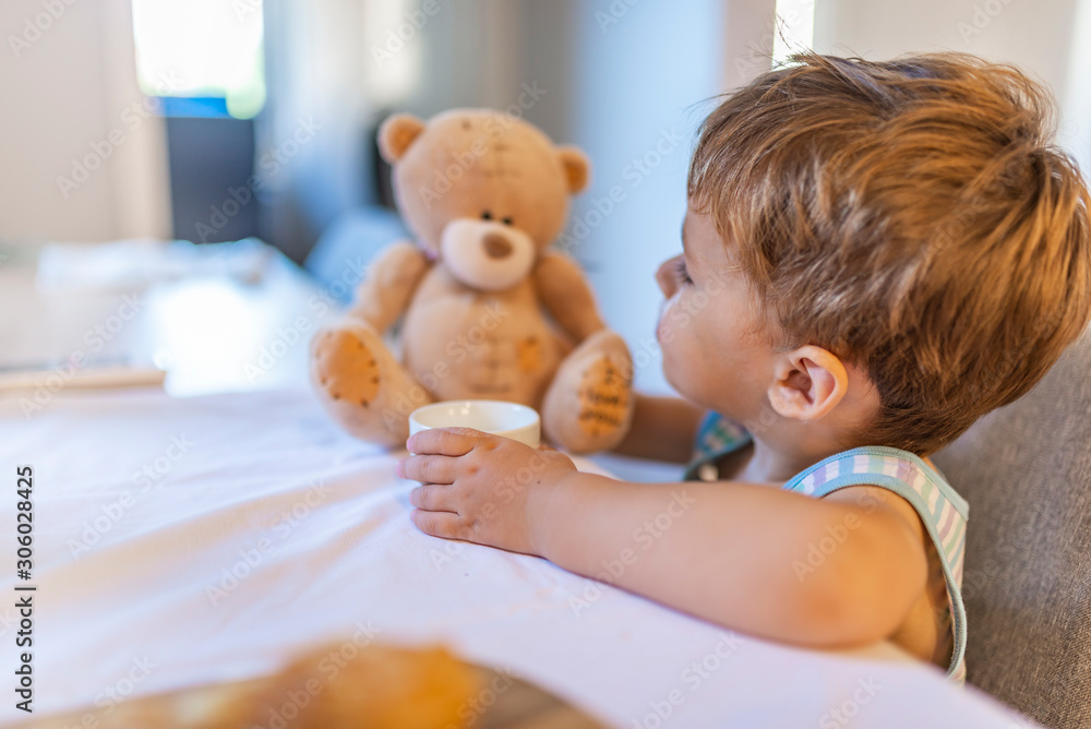 Child having breakfast. Kid feeding teddy bear toy, drinking milk and ...
