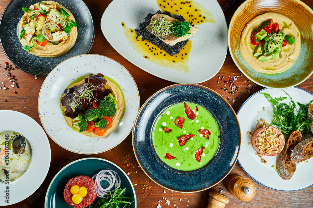 Dining table with a bunch of food. Green cream soup, hummus, dorado ...
