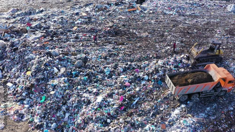 Tractor picks up rubbish in a pile and rams. Top view of a huge dump of ...
