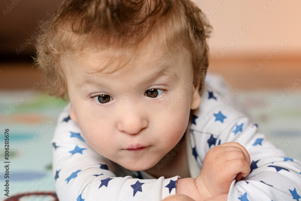 Portrait of a baby with cerebral palsy lying on his belly and playing ...