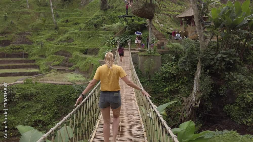 Beautiful white woman crossing the old primitive rope bridge. Bali ...