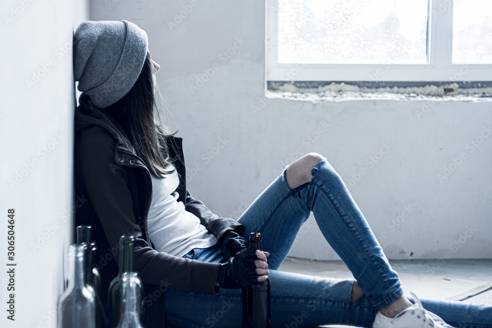 Homeless drunk young woman in hat is sitting on floor in abandoned ...