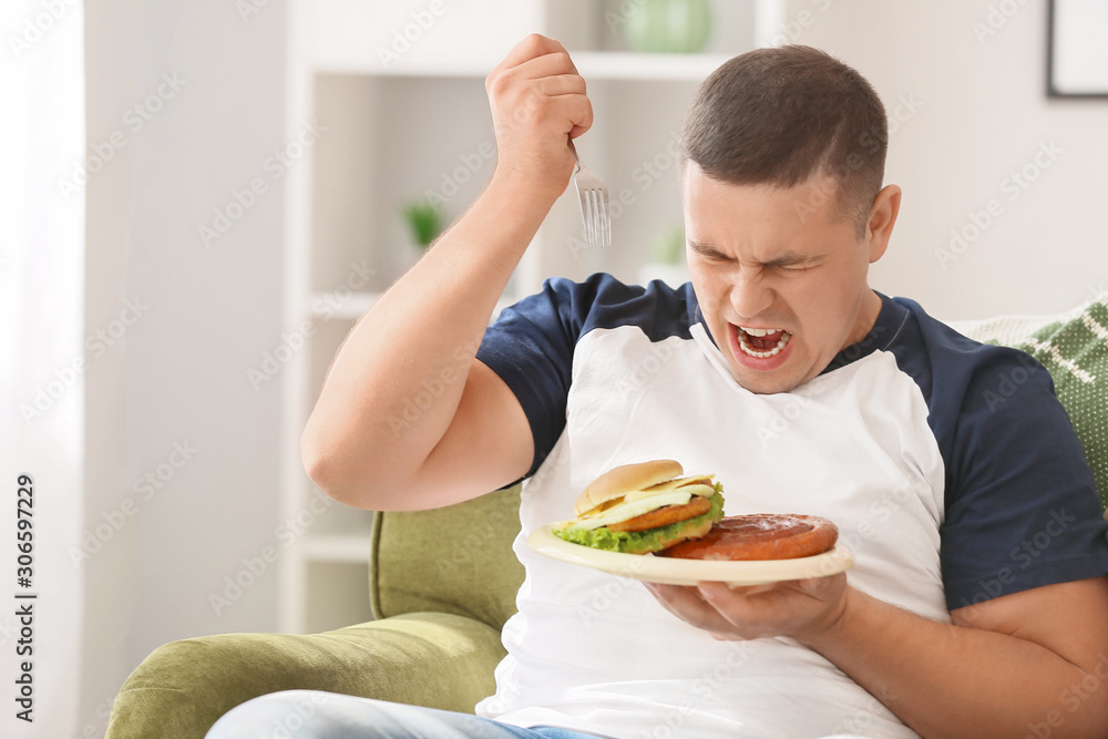 Overweight man eating unhealthy food at home Stock Photo | Adobe Stock