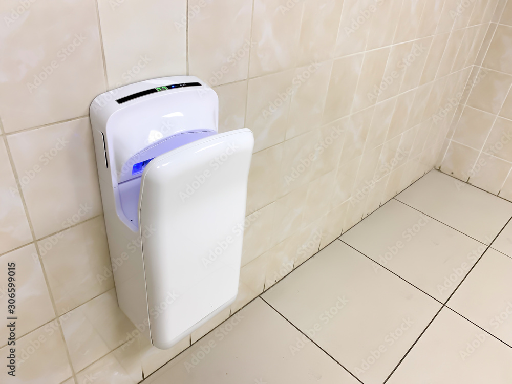 White modern hand dryer with blue lighting hanging on the wall in a ...