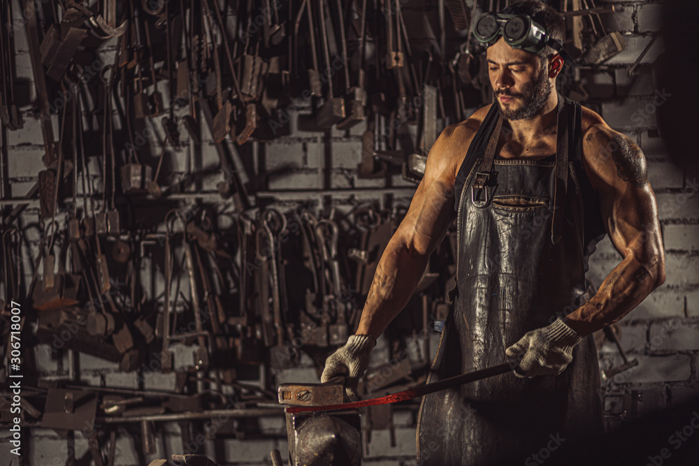 young muscular blacksmith man manually forging the molten metal ...