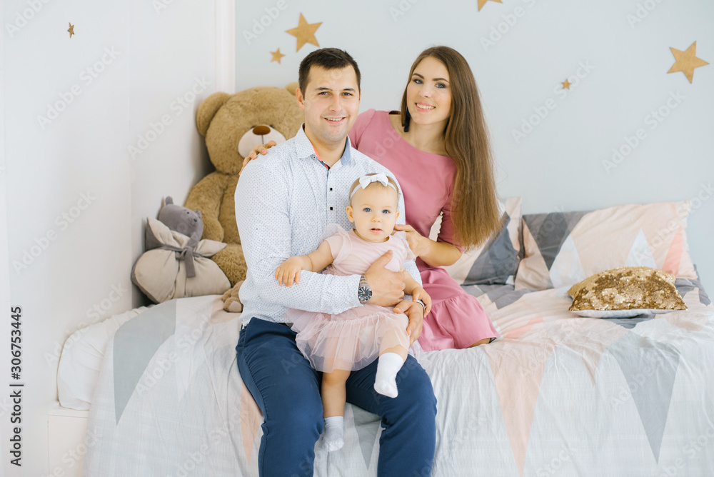 Happy family of three sitting on a baby bed in the nursery and hugging ...