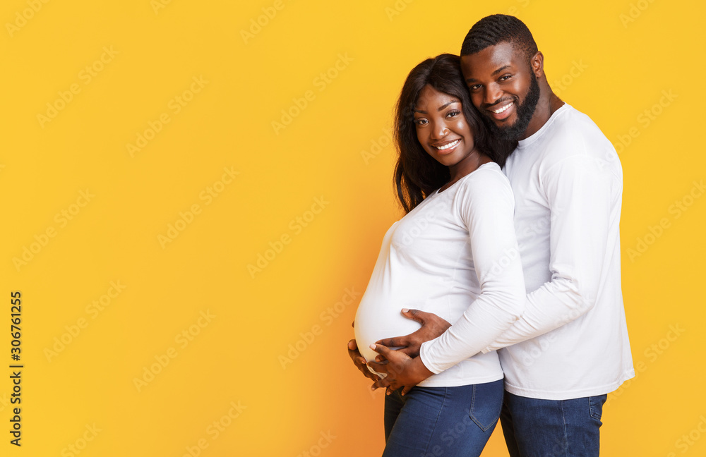 Pregnant afro woman and her husband embracing over yellow background ...