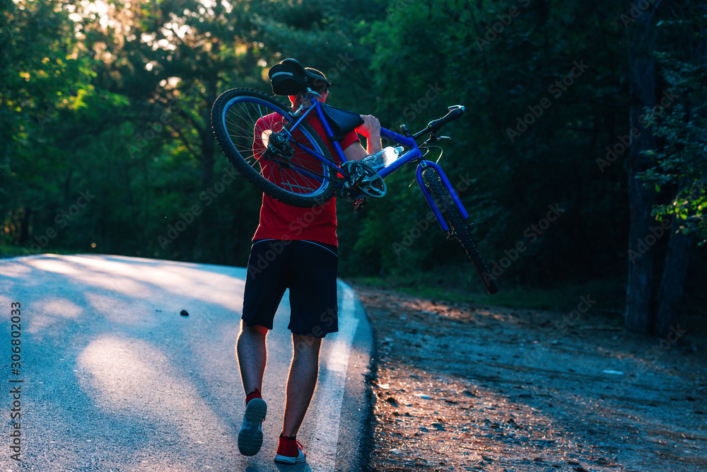 Strong athlete cyclist ( biker ) carrying his bicycle on his back on an ...