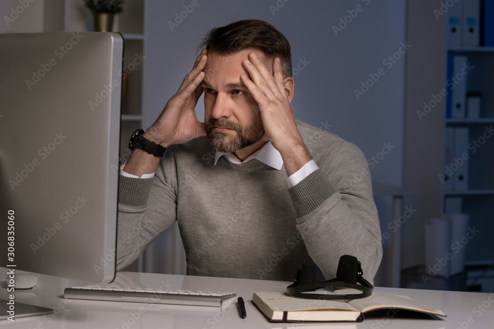 Serious and troubled office worker touching head in front of computer ...