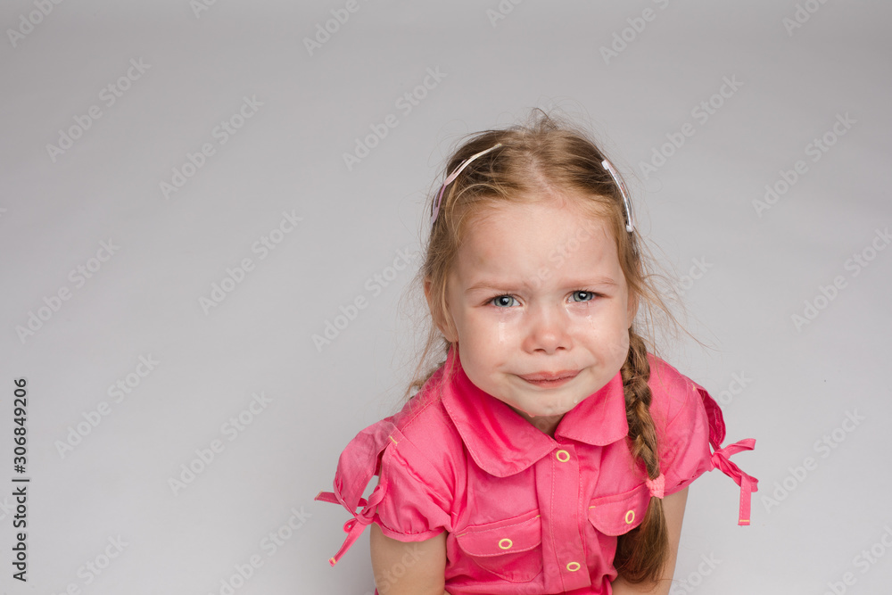Little girl in pink shirt looking aside and crying on isolated ...