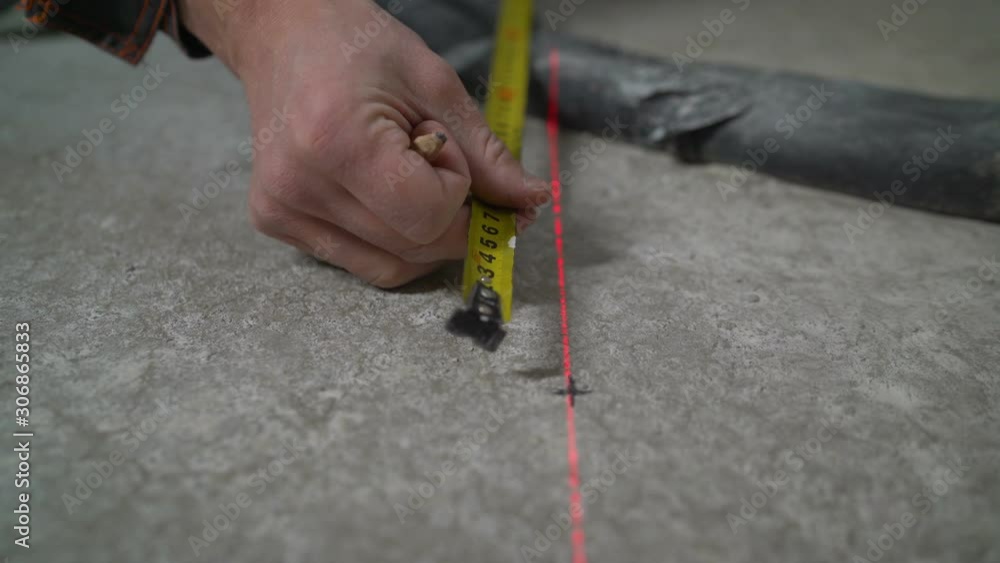 Floor repair. A worker with a tape measure makes marks on a concrete ...