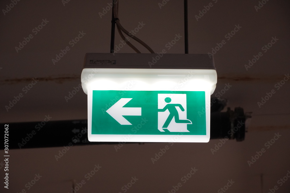 Glowing Emergency exit sign with left arrow at a building. Safety first ...