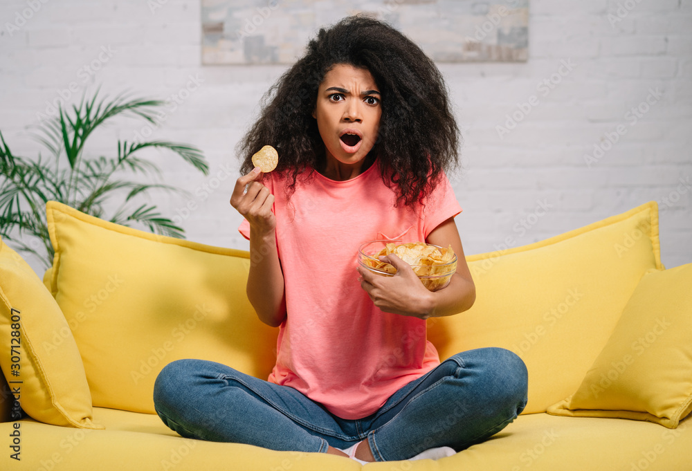 Young beautiful girl with funny emotional face eating potato chips ...