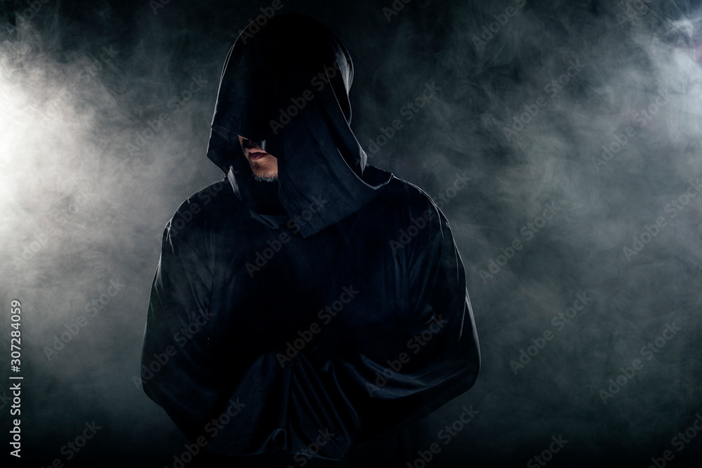 Man dressed in a dark robe looking like a cult leader on a smoky or ...
