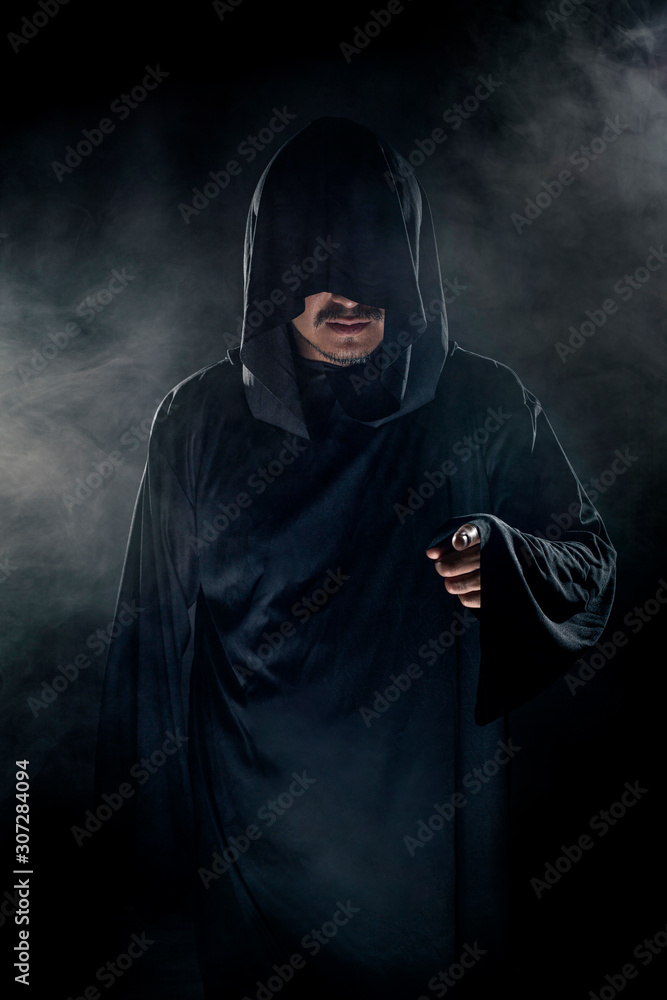 Man dressed in a dark robe looking like a cult leader on a smoky or ...
