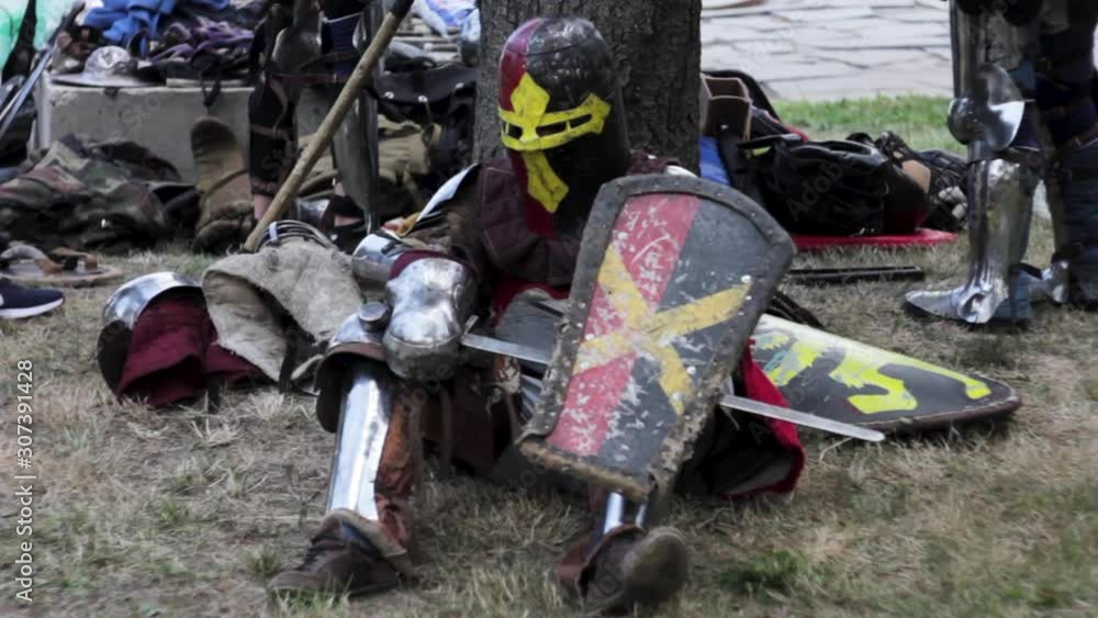 A warrior in black armor with a sword and shield in his hands sits on ...