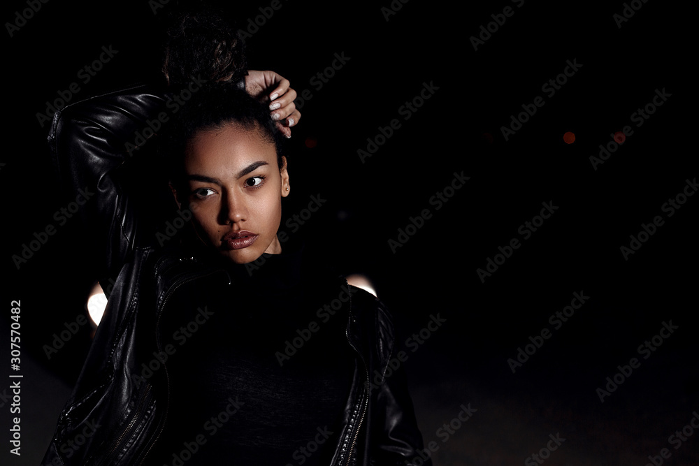 a young mulatto girl in a leather jacket and black clothes poses on an ...