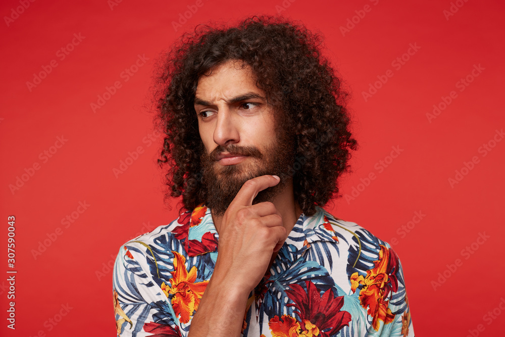 Studio photo of pensive young brunette curly male with lush beard ...