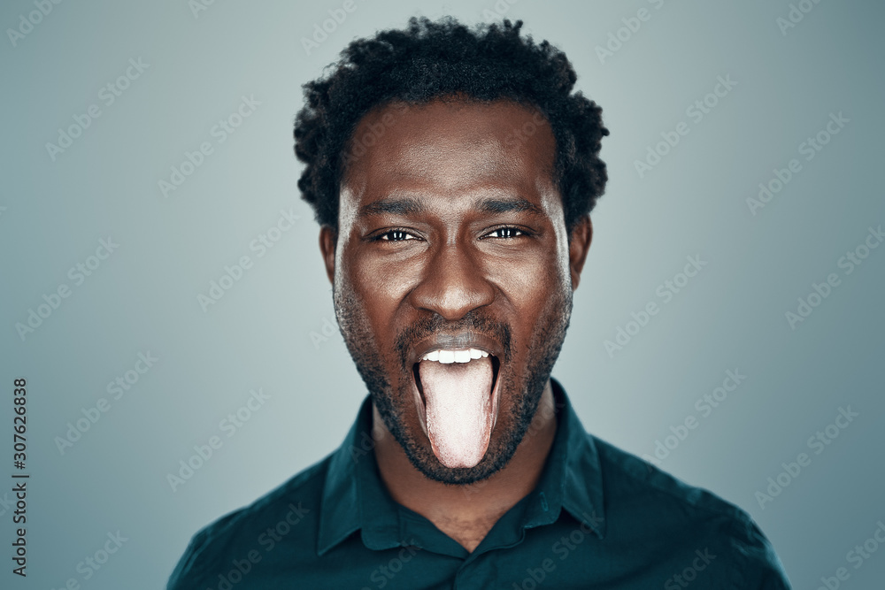 Handsome young African man looking at camera and sticking out tongue ...