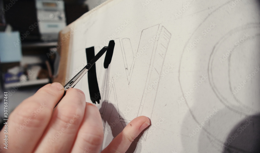 An artists hand with a paint brush painting retro letters and ...