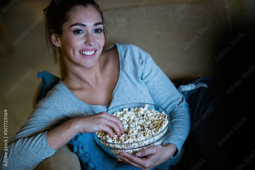 Smiling woman eating popcorn while watching movie in the evening at ...