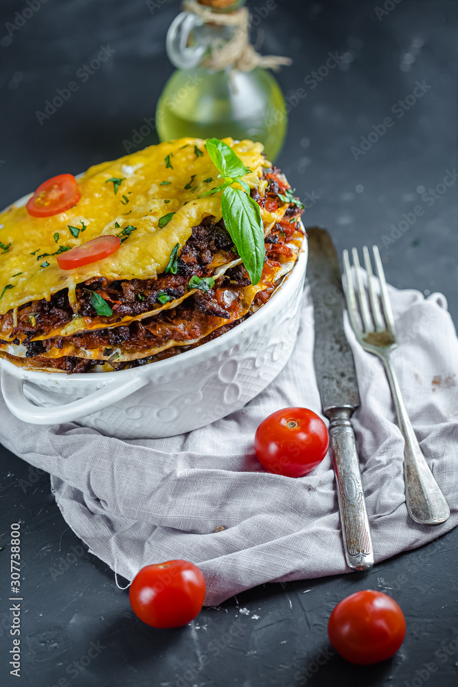 Italian lasagna in a white deep round clay pot, plate, on a black ...
