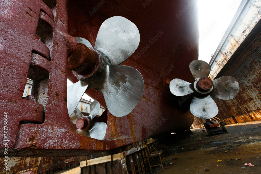 A ship stands in a dry dock in a shipyard. Large propellers of a marine ...