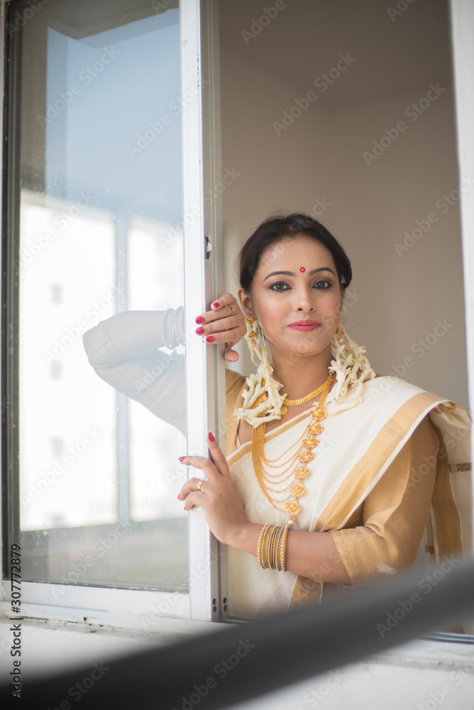 An young and attractive Indian woman in white traditional wear is ...