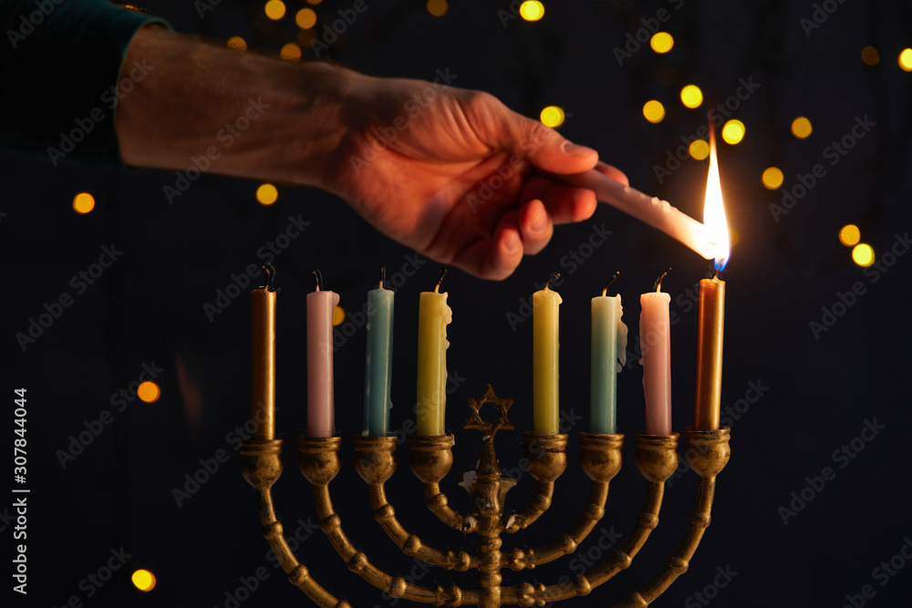 Partial view of man lighting up candles in menorah on black background ...