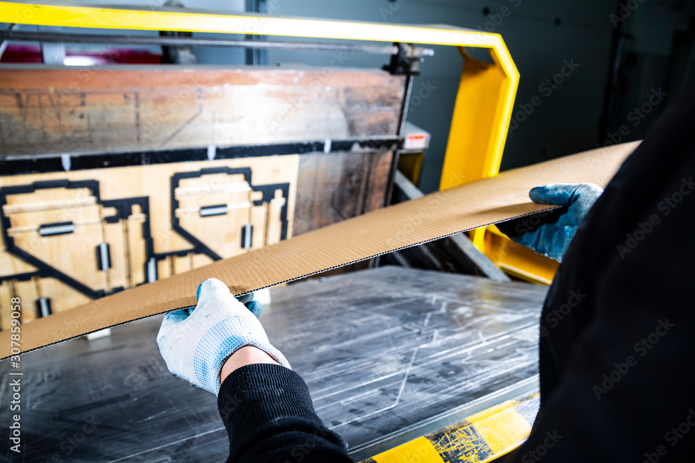 Man putting carton into a punching machine. Cardboard boxes production ...