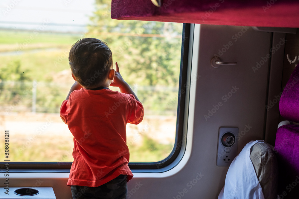 Back view of happy little boy oooking out through wide glass window of ...