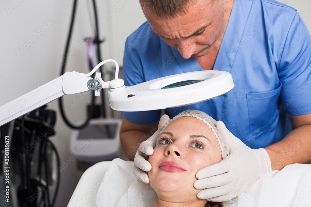 Man doctor is analysing skin on face of female patient before the ...