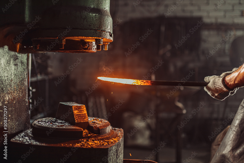 Young forger shaping metal on a jackhammer in the blacksmith workshop ...