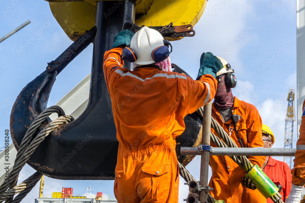 Offshore workers installing a heavy lifting sling onto a crane hook on ...